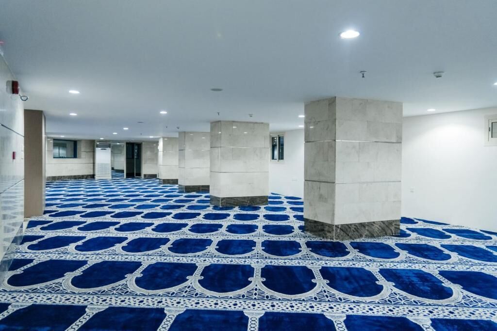 Um corredor amplo com carpete azul estampado e colunas brancas.