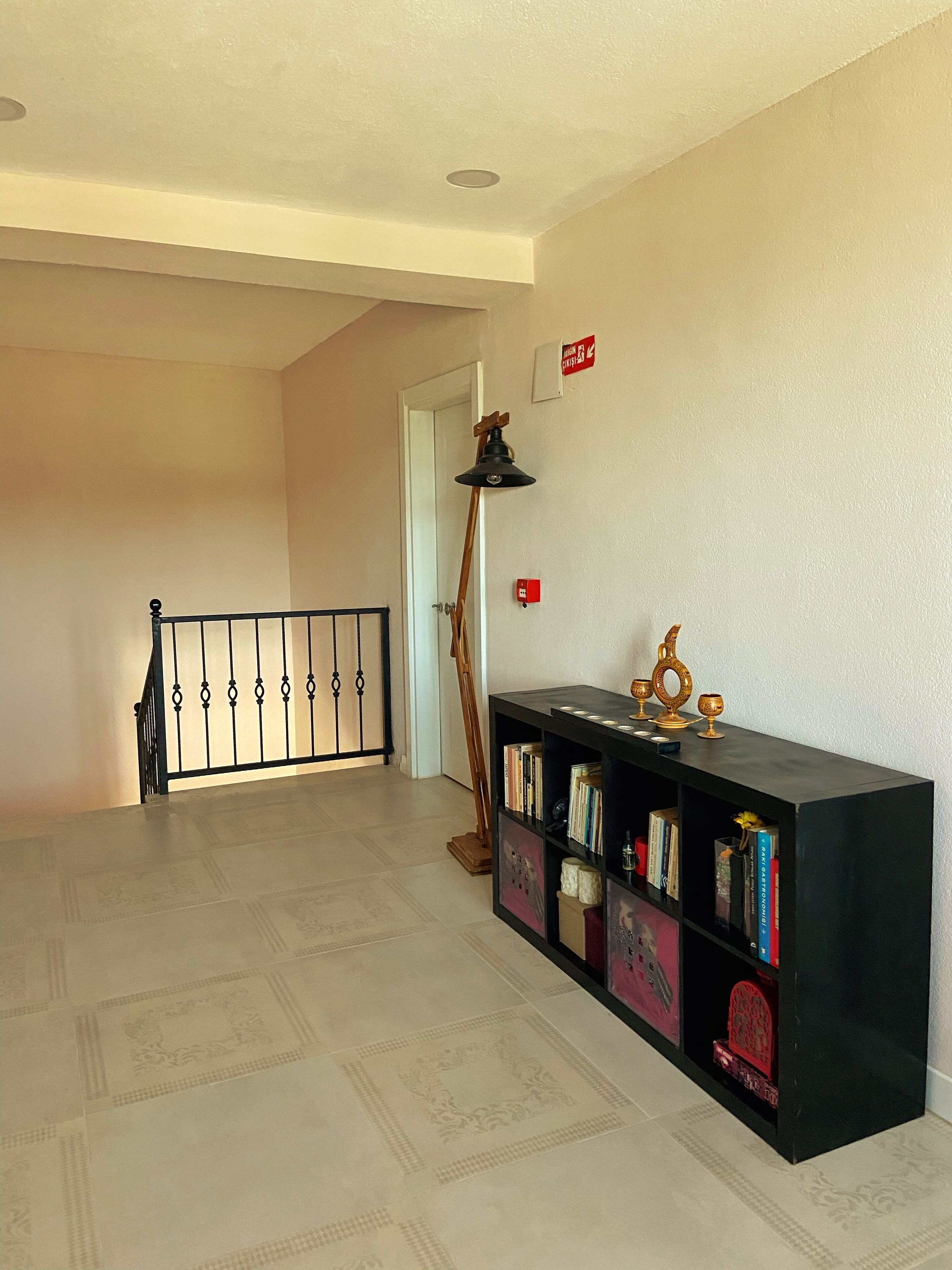 Um corredor com uma mesa consola preta, estantes de livros, soalho de madeira, escadas e uma porta.