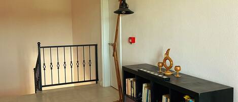 Um corredor com uma mesa consola preta, estantes de livros, soalho de madeira, escadas e uma porta.