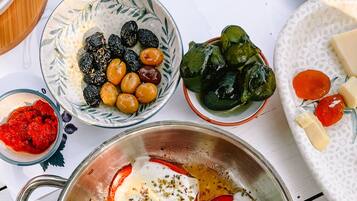 Diversos pratos, incluindo uma panela com queijo e tomate, tigelas de azeitonas e picles, e um prato com queijo e tomate.