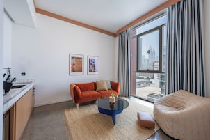 Uma sala de estar moderna com um sofá, uma mesa de centro e vista para um horizonte urbano através de grandes janelas.