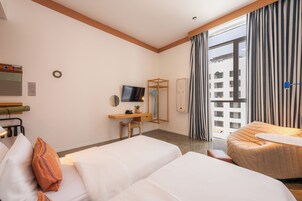 Quarto de hotel com cama, escrivaninha, televisão e vista para a cidade pela janela.
