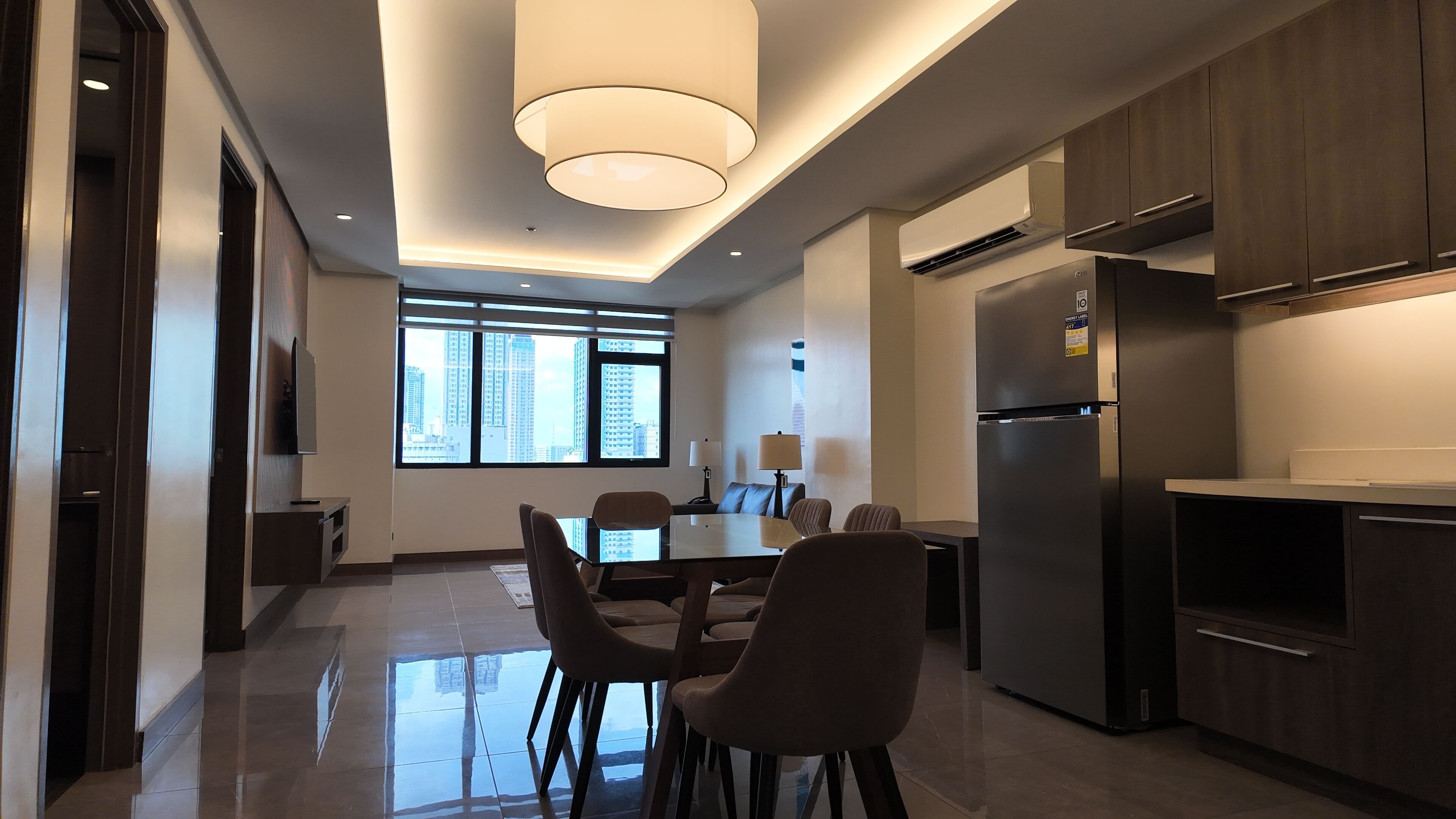 Cozinha moderna com geladeira embutida, área de refeições com mesa e cadeiras, e vista para prédios altos pela janela.