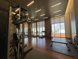 Uma academia com equipamentos de ginástica, janelas amplas e vista para o horizonte da cidade.