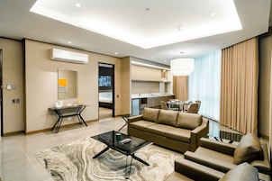 Quarto de hotel moderno com área de estar, mesa de jantar, cozinha e uma grande janela com cortinas.