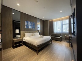 Quarto de hotel moderno com uma cama grande, um sofá, uma escrivaninha e uma televisão.