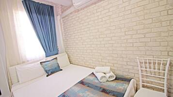 Quarto com cama, cadeira, janela com cortinas e parede de tijolos.