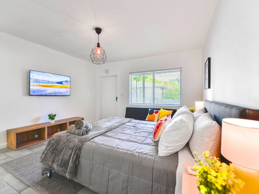 Um quarto moderno com cama, mesa de cabeceira, luminária e um quadro na parede.