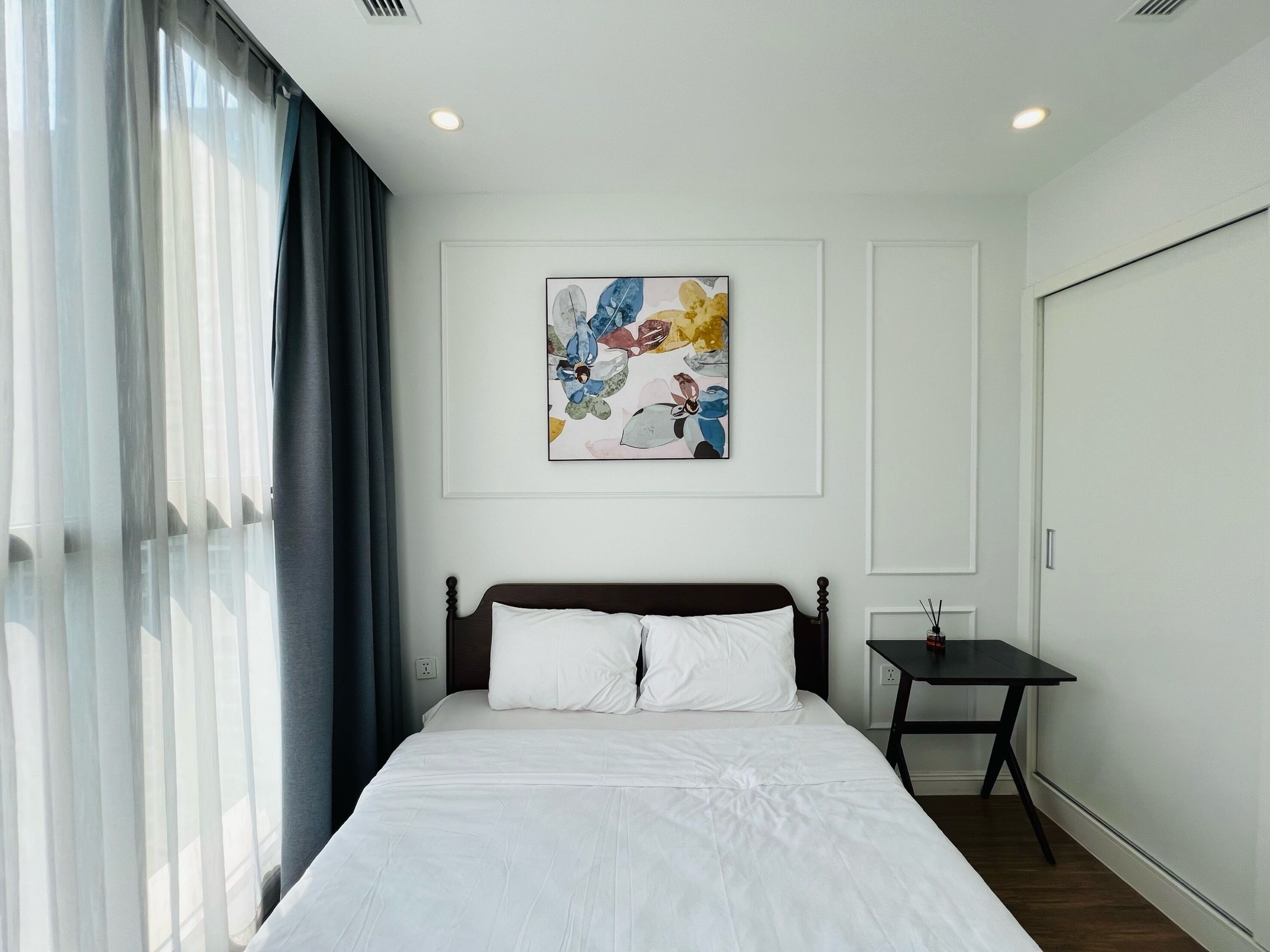 Quarto de hotel com cama, uma pequena mesa, um quadro na parede e uma janela com cortinas.