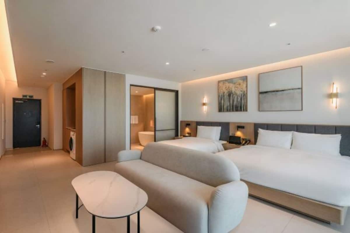 Quarto de hotel moderno com uma cama grande, um sofá, uma mesinha e banheiro com espelho e vaso sanitário.