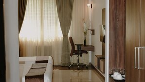 Quarto de hotel com cama, escrivaninha, cadeira, armário e banheiro.