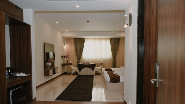 Quarto de hotel moderno com piso de madeira, área de jantar com mesa e cadeiras, um sofá e um espelho grande.