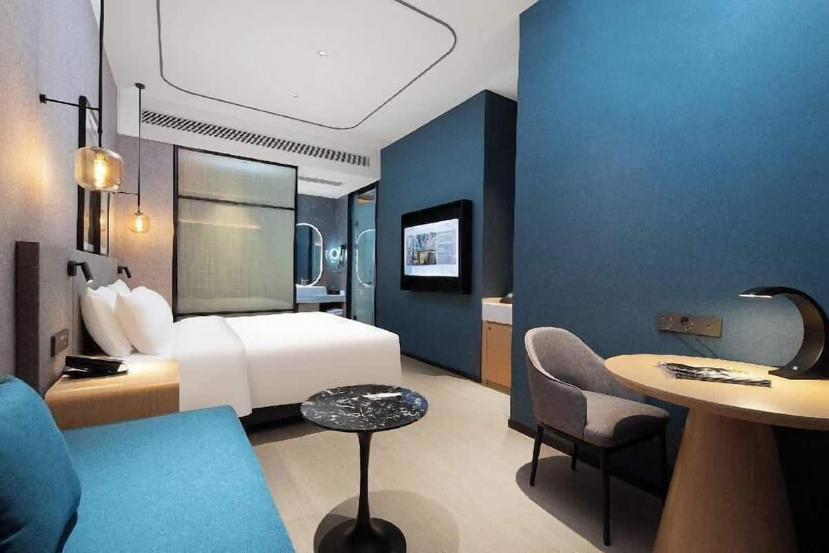 Quarto de hotel moderno com cama, escrivaninha, cadeira e televisão.