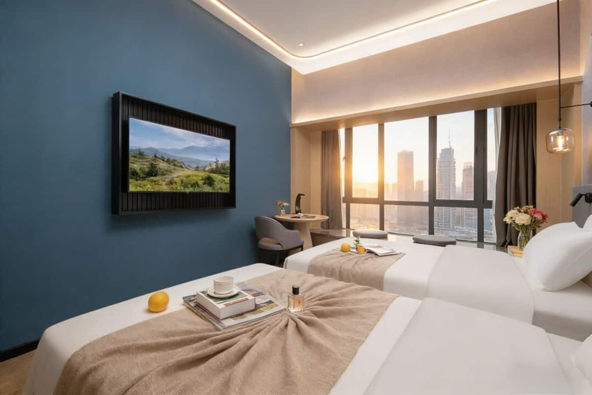 Quarto de hotel com duas camas, vista para a cidade, uma escrivaninha e uma janela grande.
