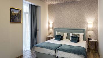 Quarto de hotel moderno com uma cama grande, duas mesas de cabeceira, um criado-mudo, uma luminária fixada na parede e um quadro emoldurado na parede.