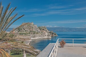 Vista costeira com um forte histórico, céu azul límpido e mar calmo.