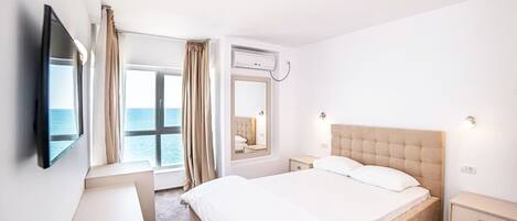 Quarto de hotel com cama grande, mesa de cabeceira, televisão fixada na parede e janela com cortinas.