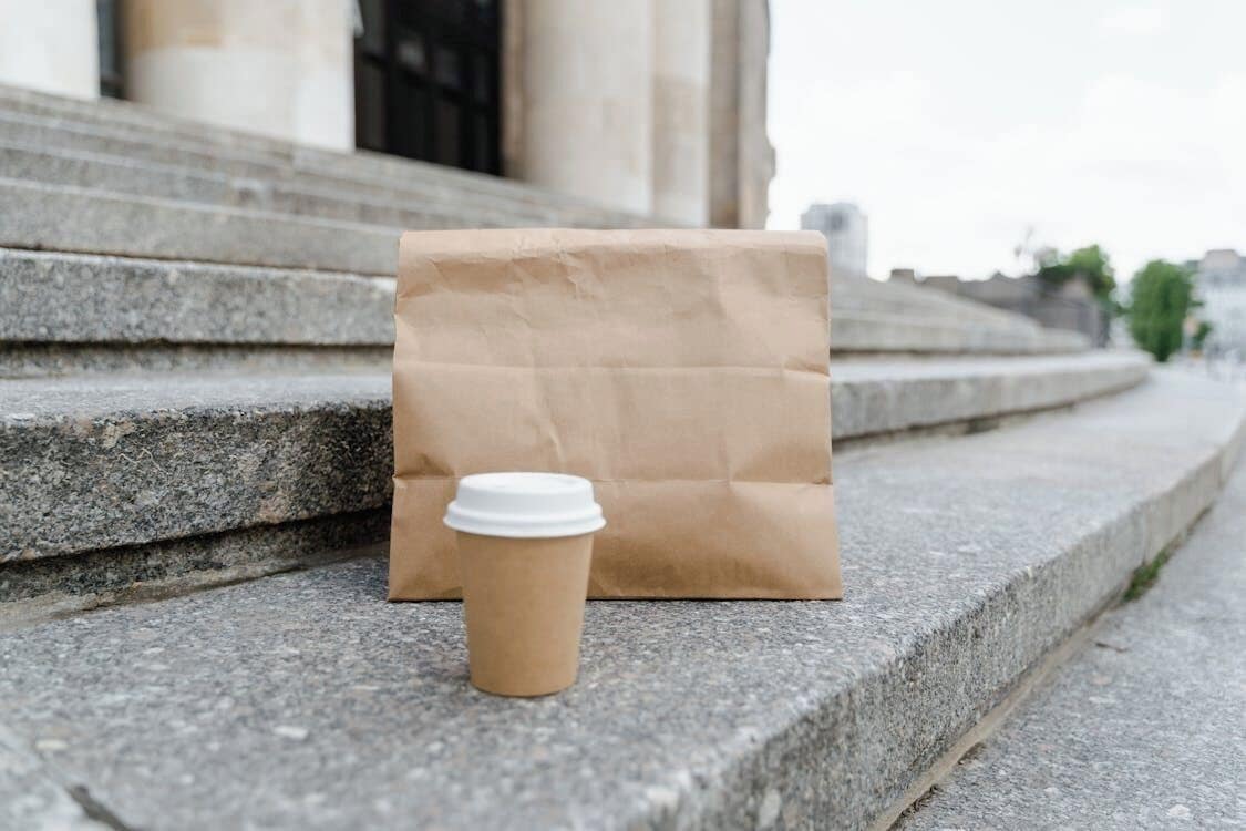 Uma chávena de café de papel e um saco de papel em degraus de pedra.