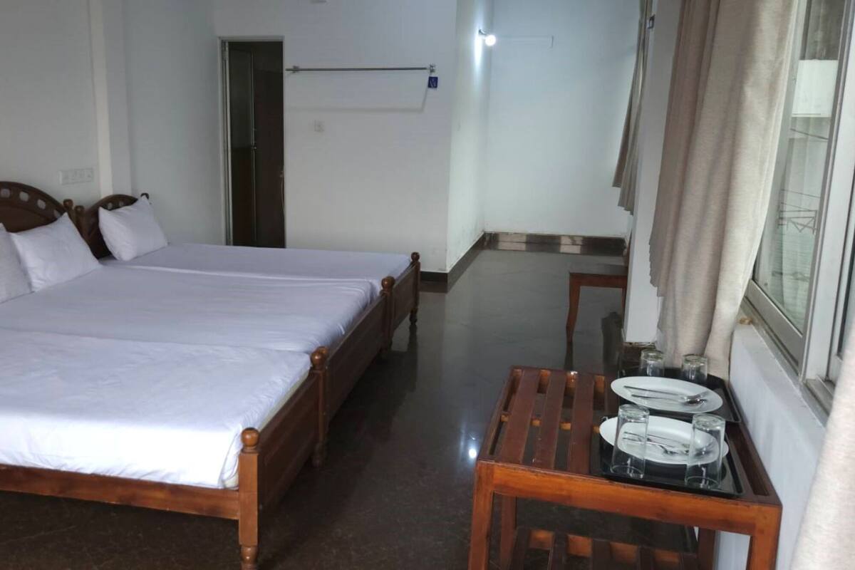 Quarto de hotel com duas camas de solteiro, uma mesa pequena com bandeja e uma janela com cortinas.