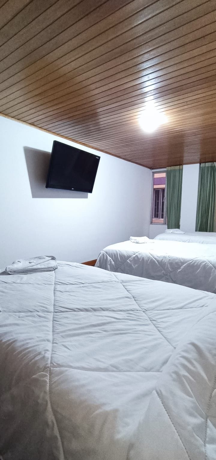 Quarto com duas camas, televisão de tela plana na parede e janela com cortinas verdes.
