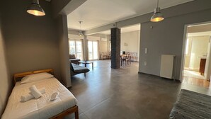 Um quarto de hotel espaçoso, com uma cama grande, um espaço de estar com um sofá e poltronas, uma área de jantar com mesa e cadeiras, e uma cozinha visível através de uma porta aberta.