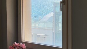 Quarto com janela que dá para a paisagem urbana, uma mesinha com uma orquídea em vaso e uma cadeira.