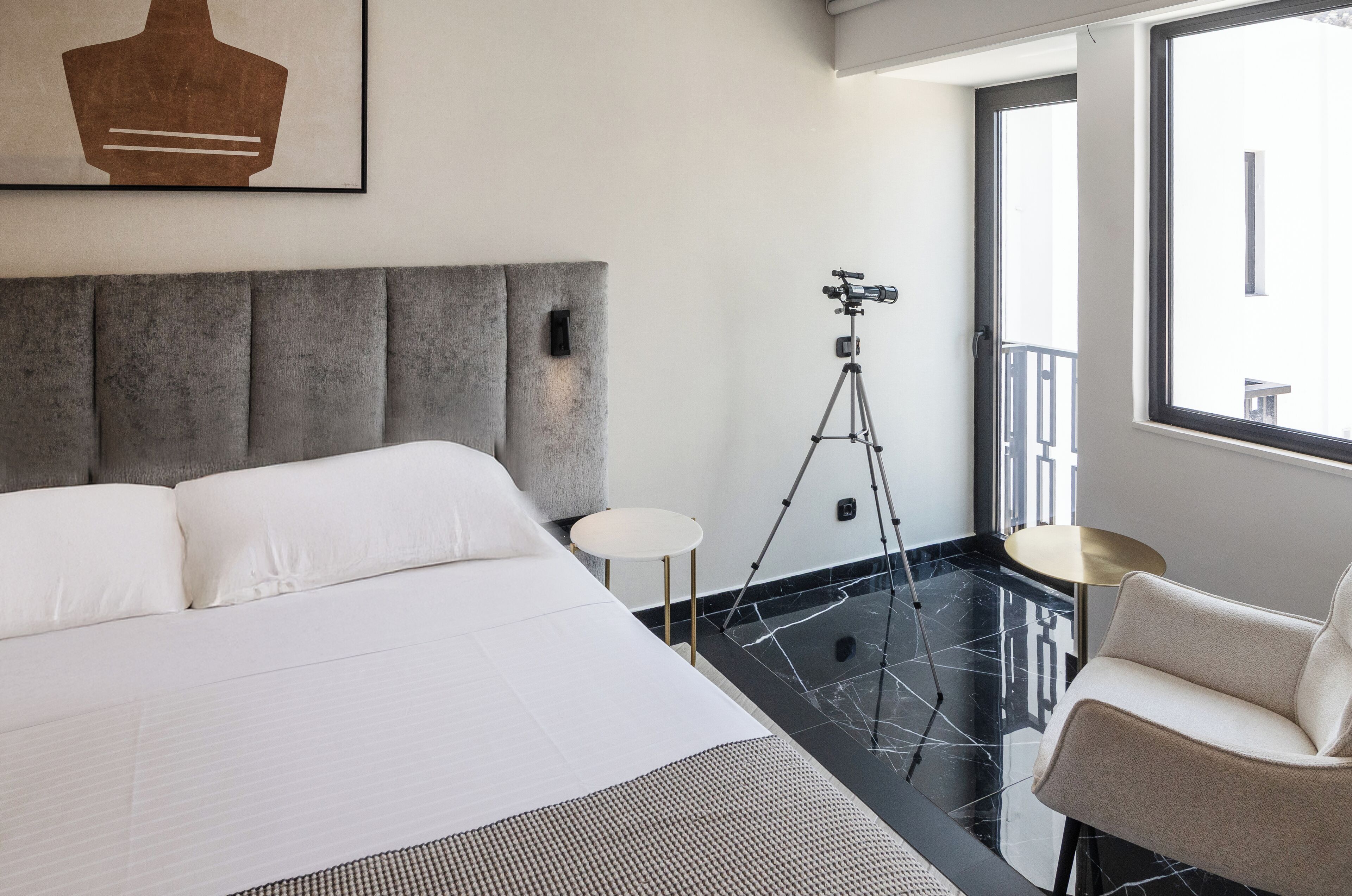Quarto de hotel moderno com uma cama grande, um tripé e uma cadeira.