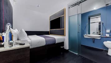 Quarto de hotel moderno com cama, mesa de cabeceira e banheiro com pia e espelho.