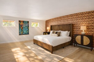 Quarto com cama de madeira, duas mesas de cabeceira com abajures, um quadro grande na parede e papel de parede estampado.