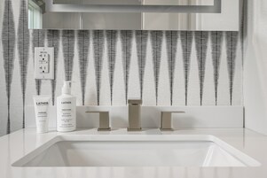 Casa de banho com lavatório branco, duas embalagens de sabonete líquido Lather e uma torneira moderna.