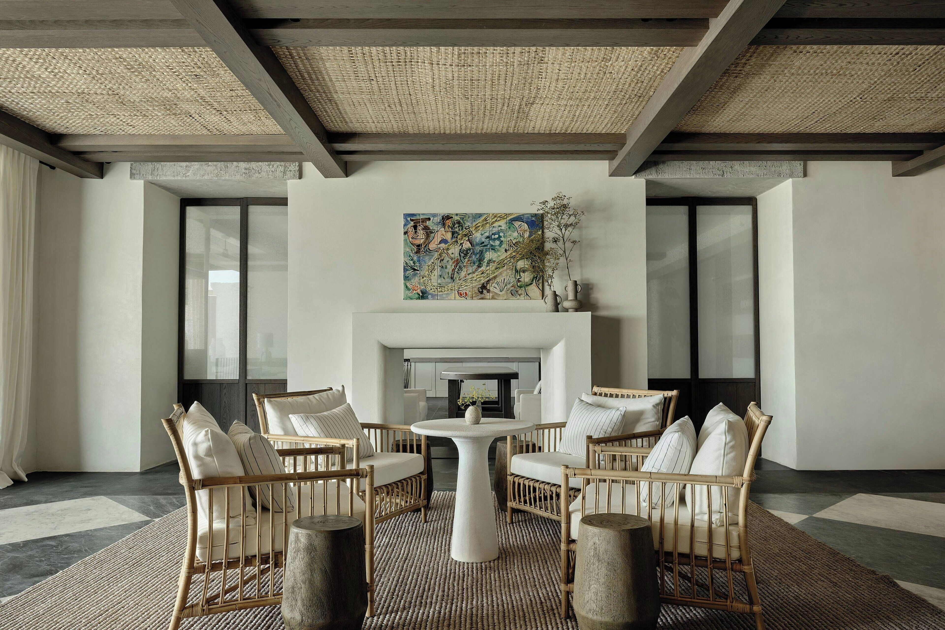 Uma sala de estar moderna com uma mesa redonda central, cadeiras de vime, um grande quadro abstrato e uma lareira.