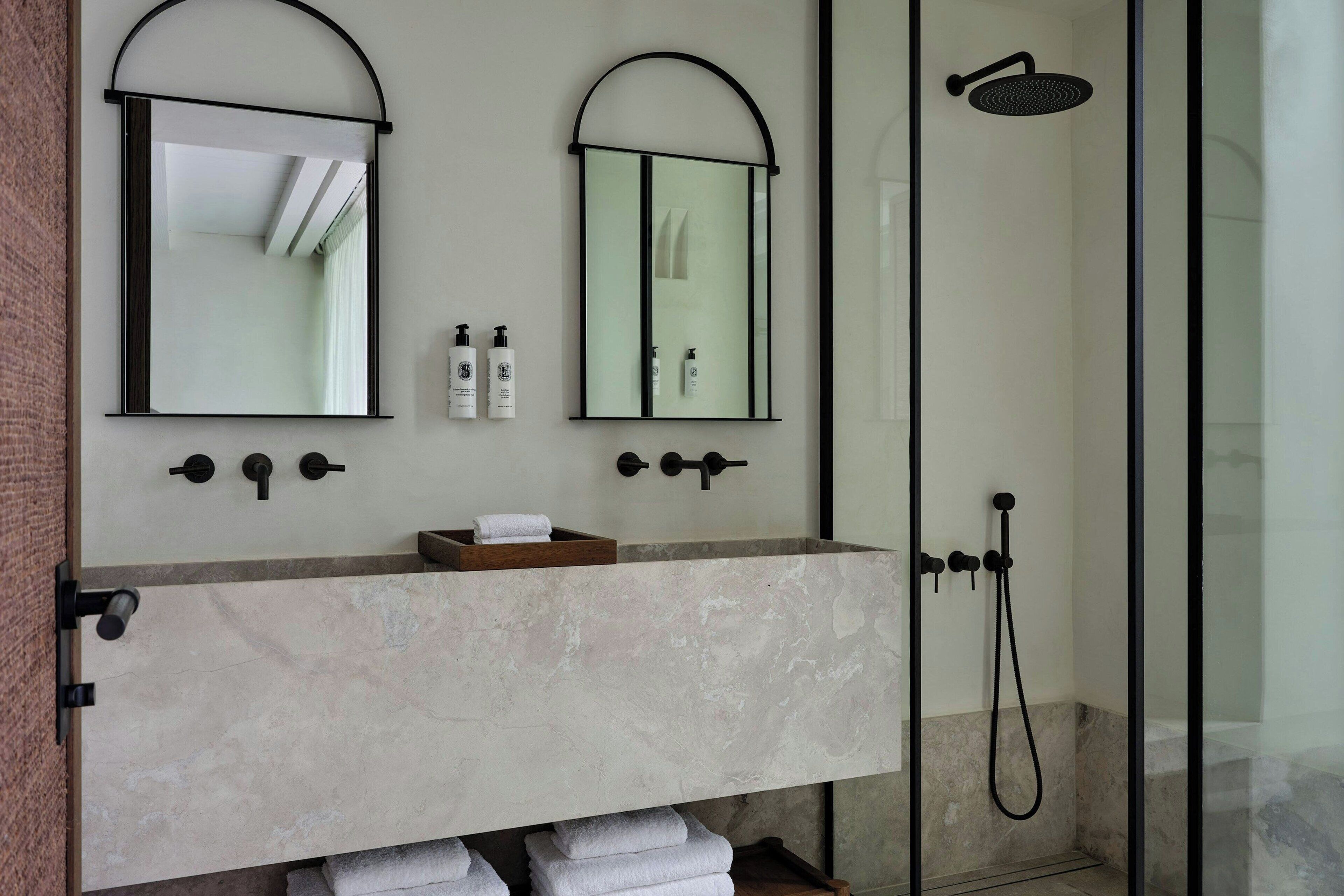 Um banheiro moderno com toucador de mármore, dois espelhos fixados na parede, box de vidro e porta-toalhas.