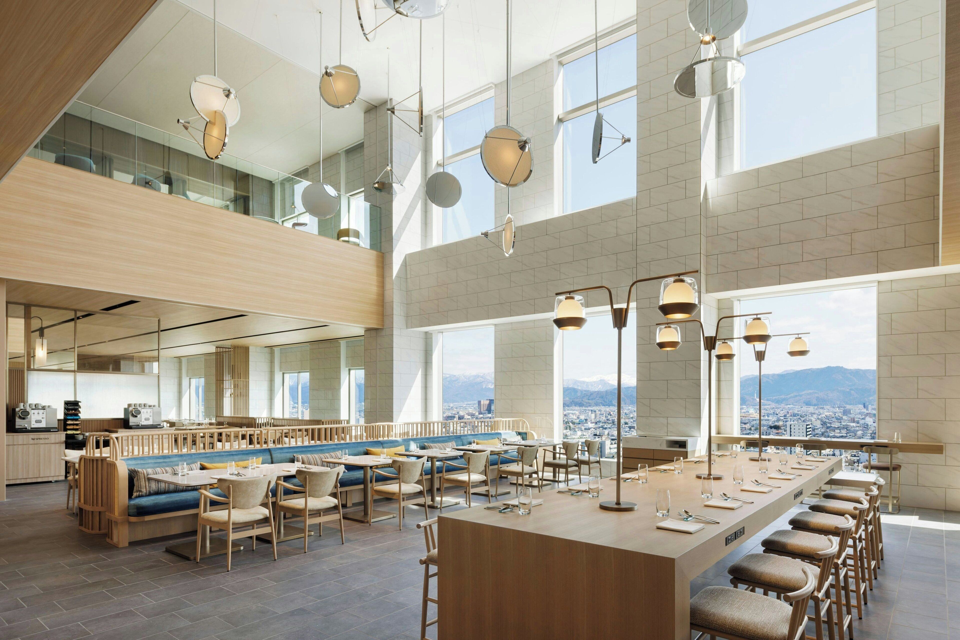 Um restaurante moderno com tetos altos, janelas amplas e uma longa área de refeições comunitária.