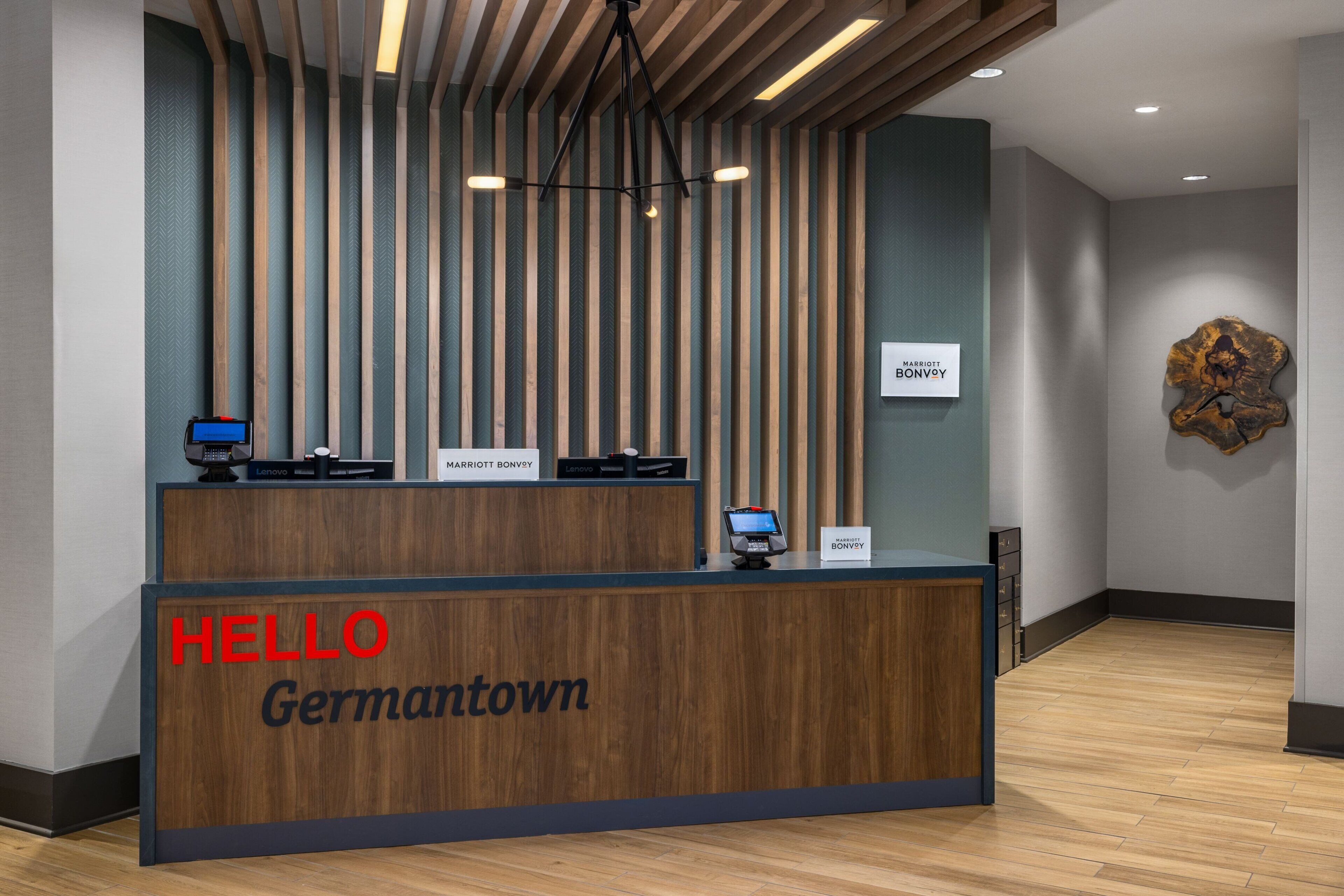 Uma receção com acabamento em madeira, um letreiro com a inscrição "HELLO Germantown" e uma luminária pendente moderna acima.