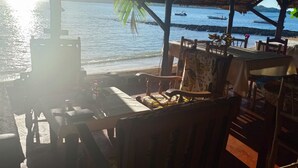 Um restaurante à beira-mar com vista para o mar, móveis de madeira e um telhado de palha.