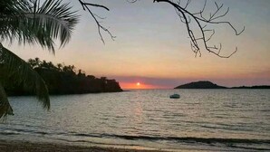 Um pôr do sol sobre um mar calmo, com um barco e palmeiras.