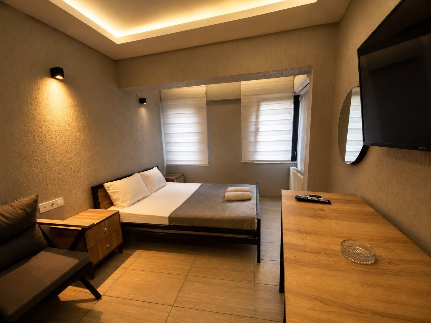 Quarto moderno com cama, mesas de cabeceira, televisão e sofá.