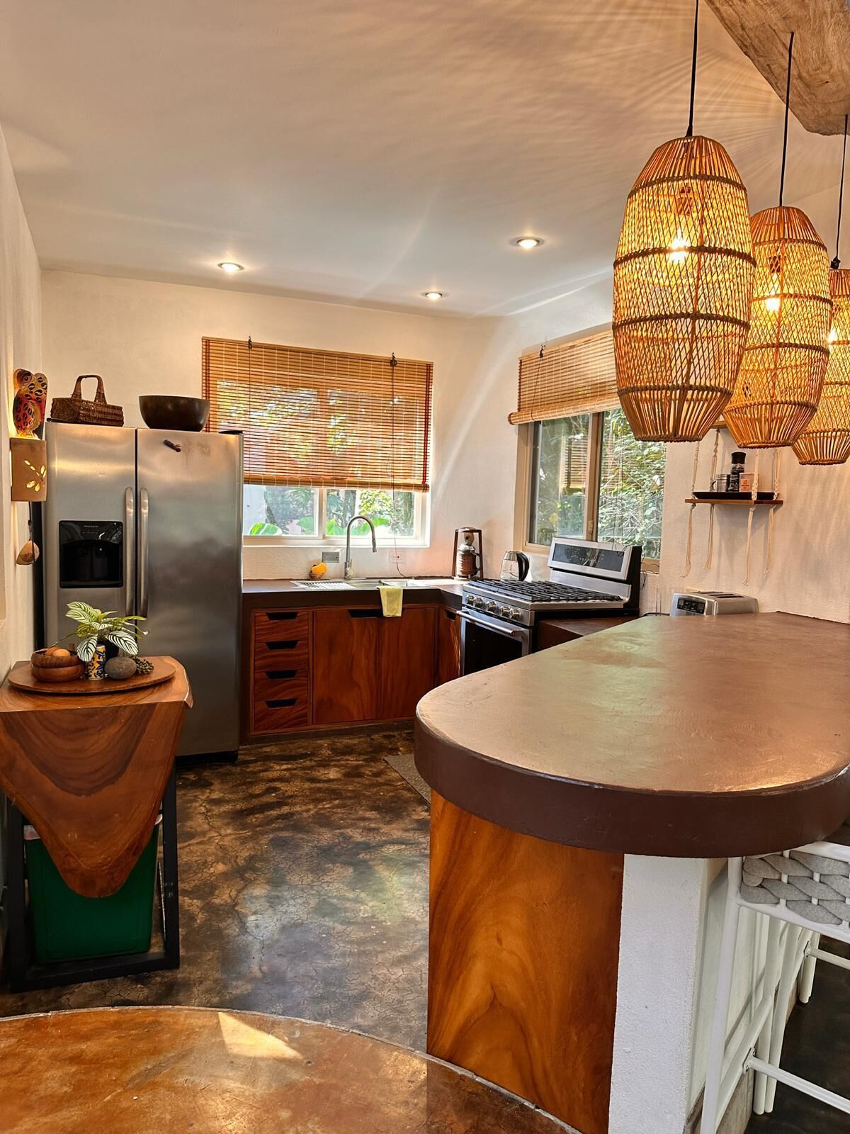 Cozinha moderna com ilha central, armários de madeira e geladeira de aço inoxidável.