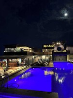 Vista noturna de um hotel com piscina, bar e um letreiro que diz 'Sky Lounge'.