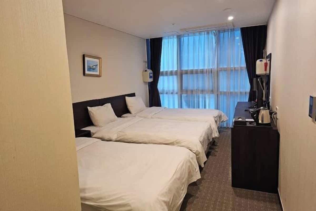 Quarto de hotel com duas camas, uma escrivaninha, uma janela com cortinas e um quadro na parede.