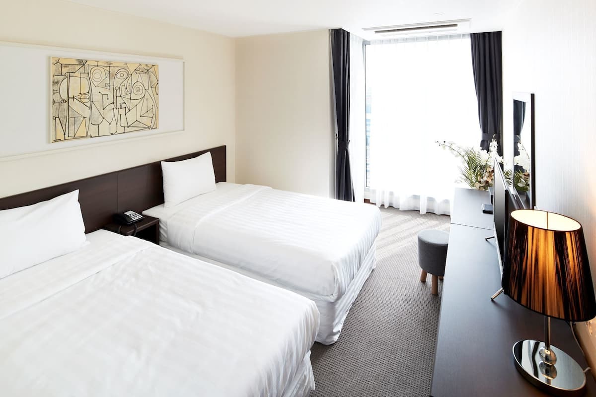 Quarto de hotel com duas camas, uma mesa com abajur, telefone e um quadro na parede.