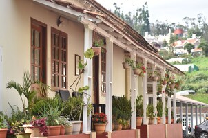 Um edifício com varanda adornada por plantas em vasos e um carro estacionado na frente.