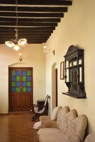 Um quarto com porta de madeira, um sofá estampado, uma mesinha e um espelho fixado na parede.