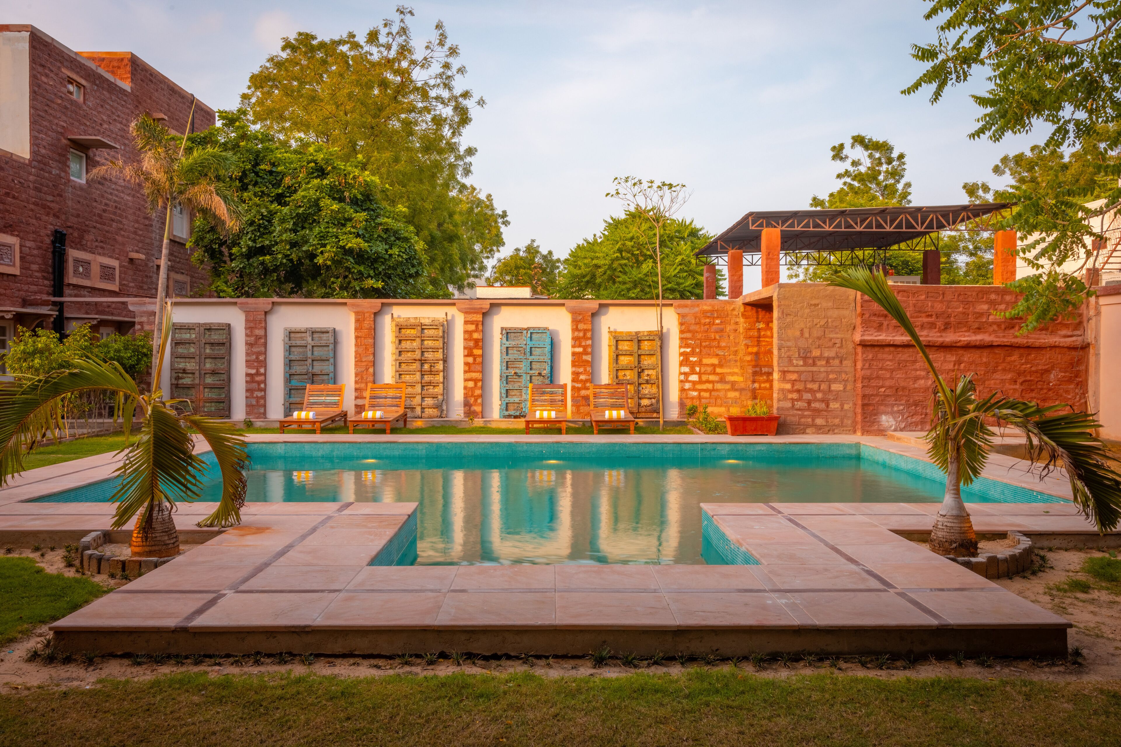 Piscina com muro de tijolos, palmeiras e espreguiçadeiras.