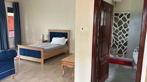 Quarto com cama, mesa de cabeceira e uma poltrona azul.