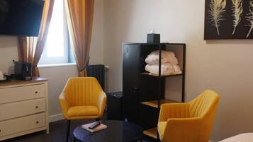Quarto de hotel com uma cama, duas poltronas amarelas, uma mesa redonda pequena, uma televisão, um guarda-roupa e um quadro na parede.