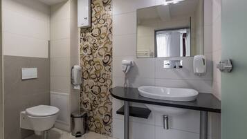 Casa de banho com sanita, lavatório, espelho e parede estampada.