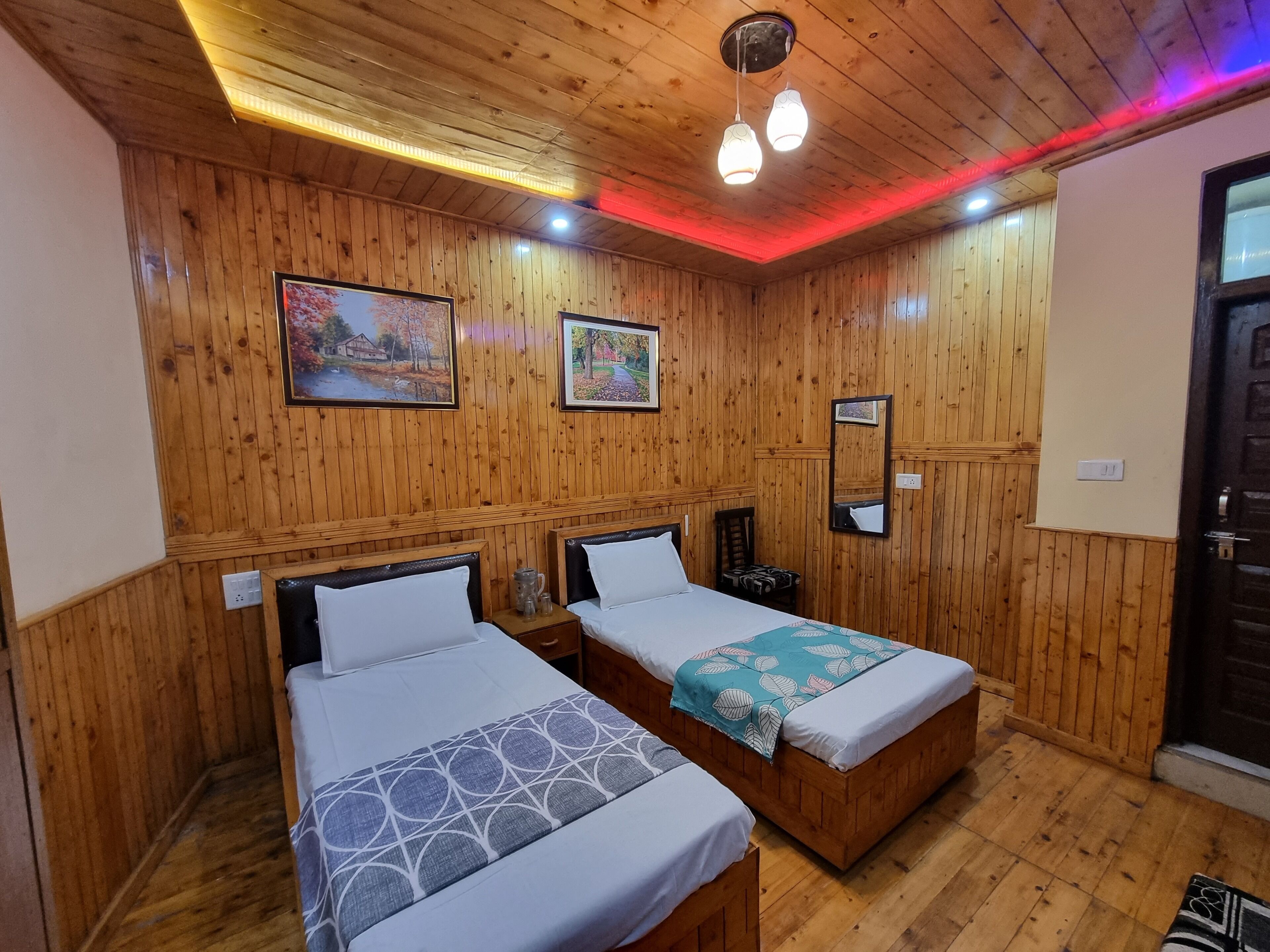 Quarto com painéis de madeira, duas camas com lençóis brancos, uma mesa pequena com um jarro e um espelho na parede.