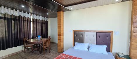 Quarto de hotel com teto de madeira, cama com colcha estampada, mesa de cabeceira com telefone e pequena mesa de madeira com cadeiras.