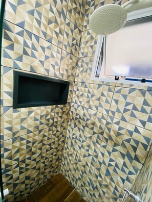 Casa de banho com azulejos estampados, um chuveiro e uma pequena prateleira.